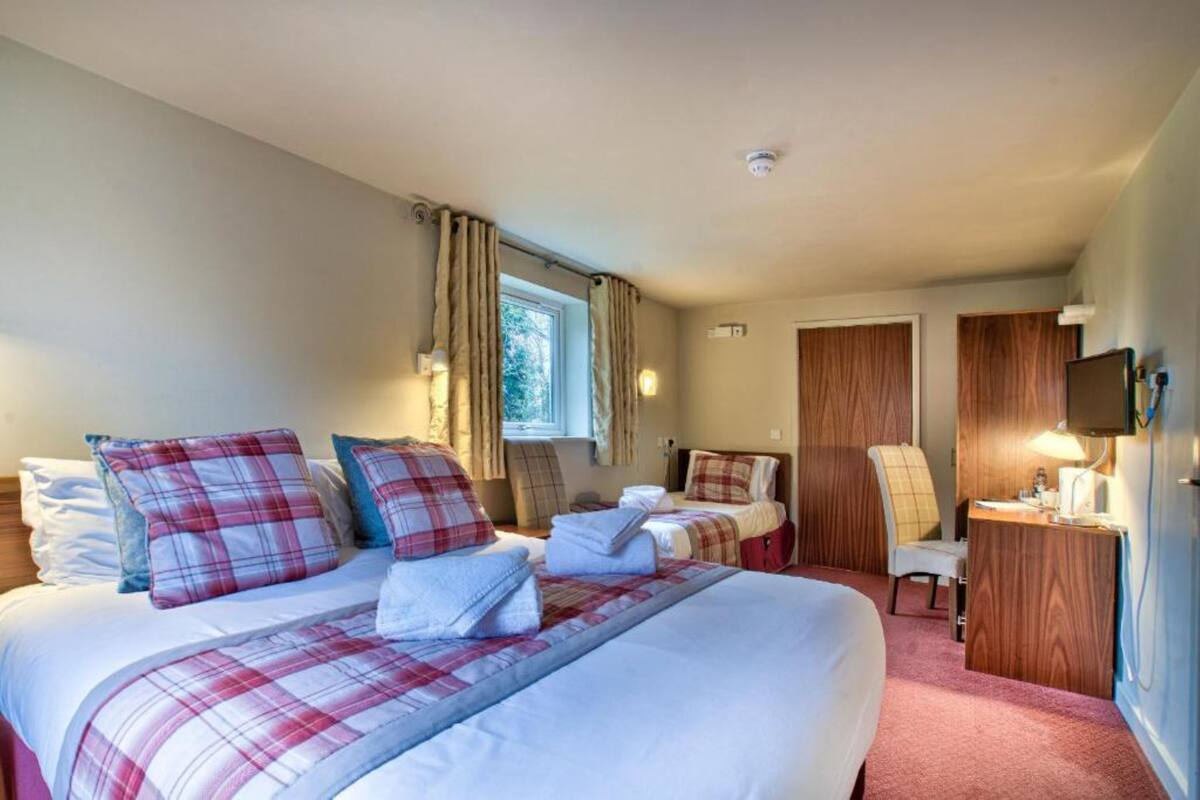Quarto de hotel com duas camas, uma escrivaninha, uma cadeira e uma televisão.
