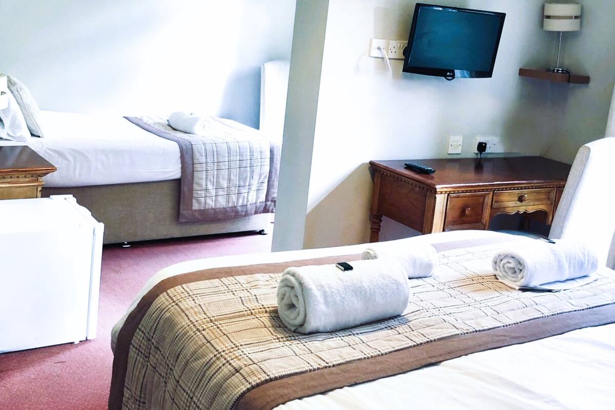 Quarto de hotel com cama, escrivaninha, televisão e uma cadeira.