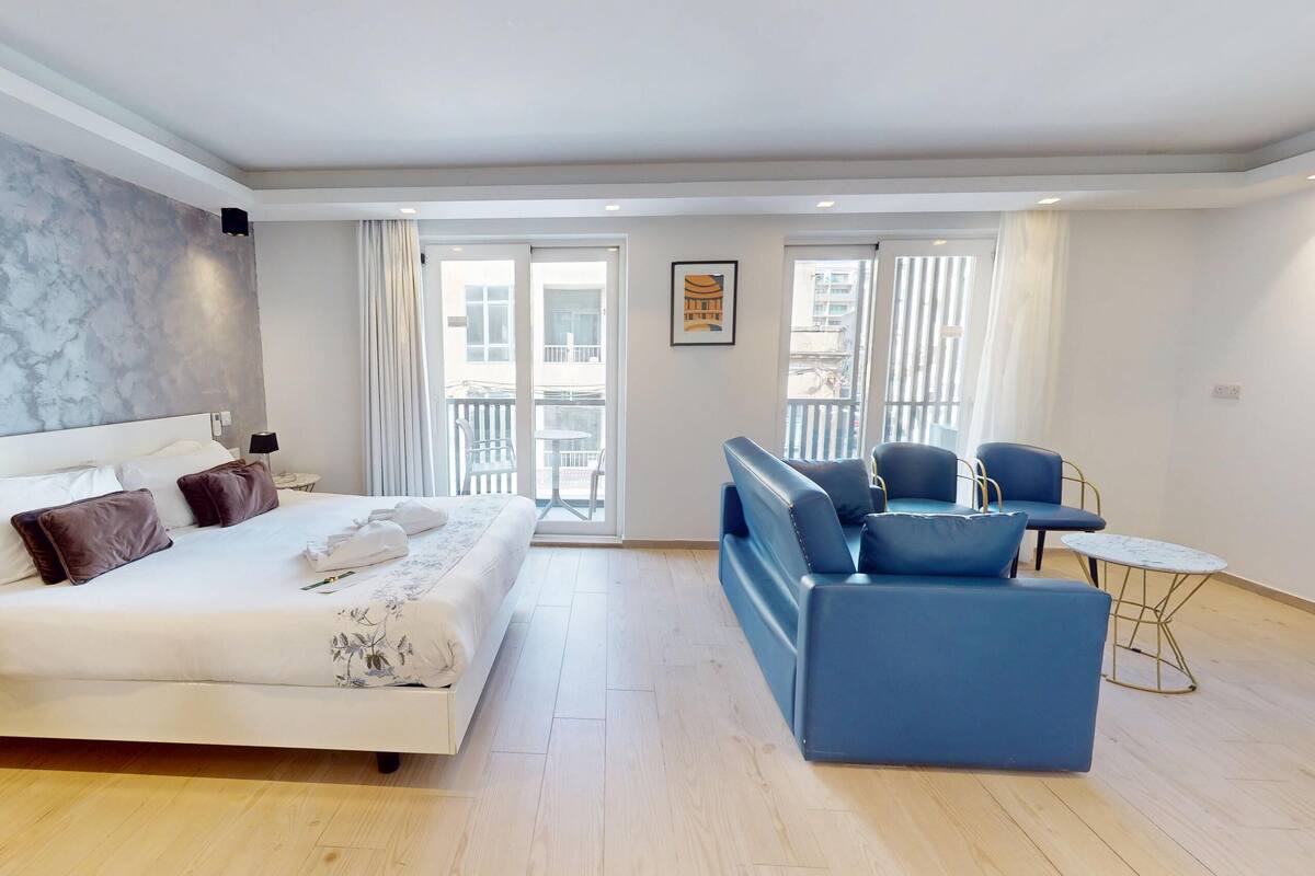 Quarto moderno com cama, sofá, mesinha e varanda com vista.