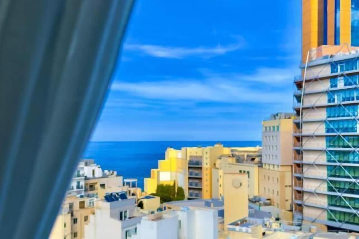 Paisagem urbana com edifícios modernos, incluindo uma estrutura alta com detalhes em amarelo e azul.
