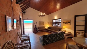 Uma sala de estar espaçosa com teto de madeira, parede de tijolos e vista para o exterior. Há dois sofás, uma mesa e uma cadeira.