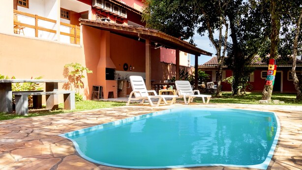 Piscina com espreguiçadeiras, um pátio de pedra e um edifício com fachada vermelha e varanda.