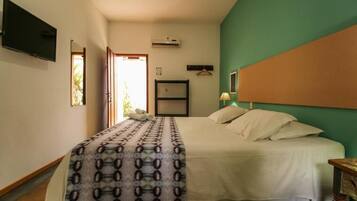 Quarto com uma cama, televisão na parede, ar condicionado e porta que dá para outro cômodo.