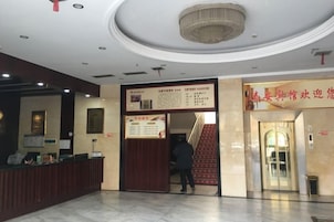 Um saguão de hotel com balcão de recepção, escada e lustre.