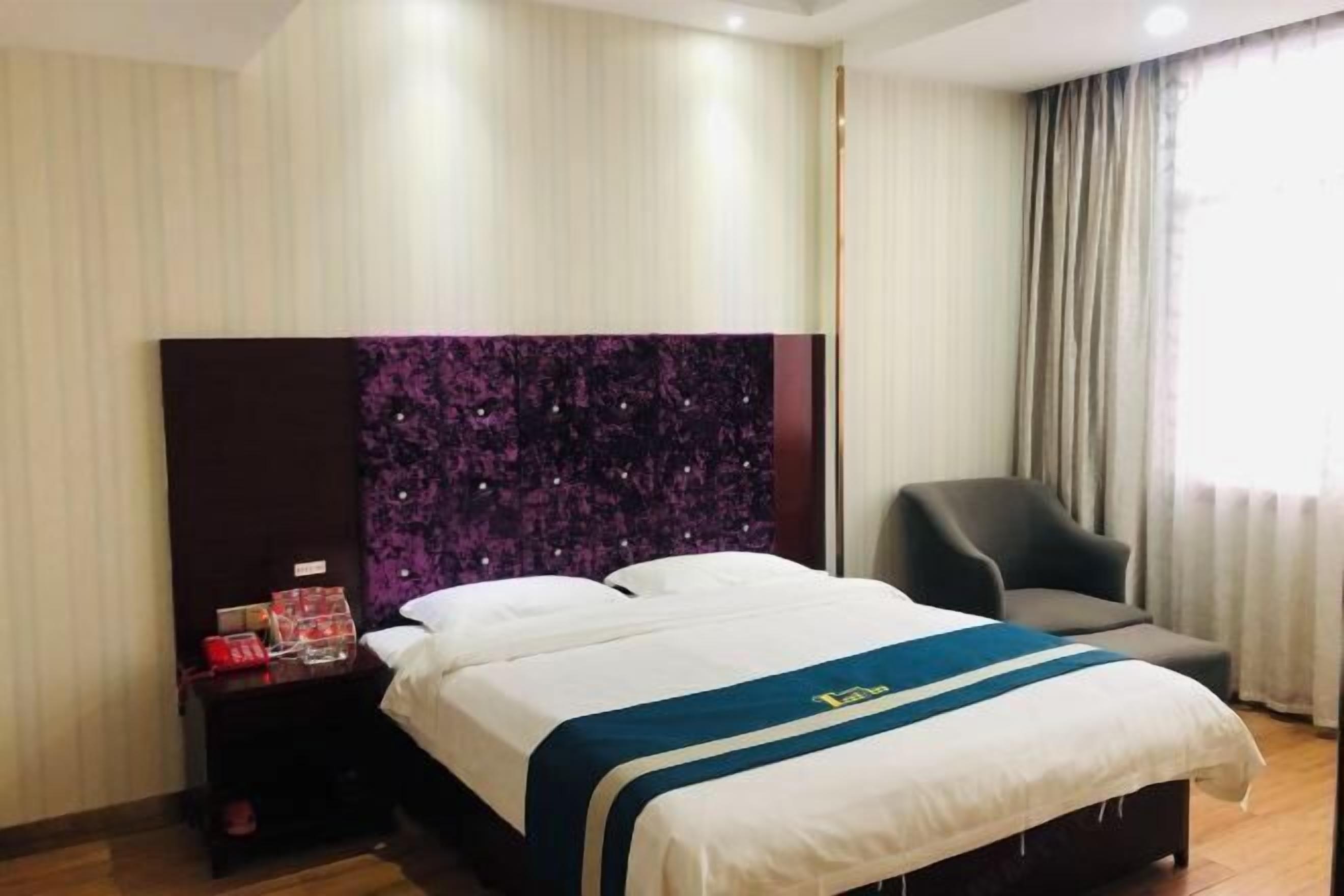 Quarto de hotel com cama, mesa de cabeceira, cadeira e janela com cortinas.