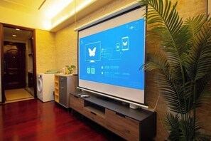 Quarto com uma televisão de tela grande presa a um suporte de madeira, uma máquina de lavar roupa e um vaso de planta.