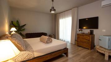Quarto com cama, luminária de cabeceira, cômoda, televisão e uma planta.
