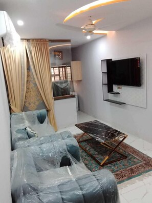 Uma sala de estar moderna com um sofá, uma televisão na parede e um ventilador de teto.