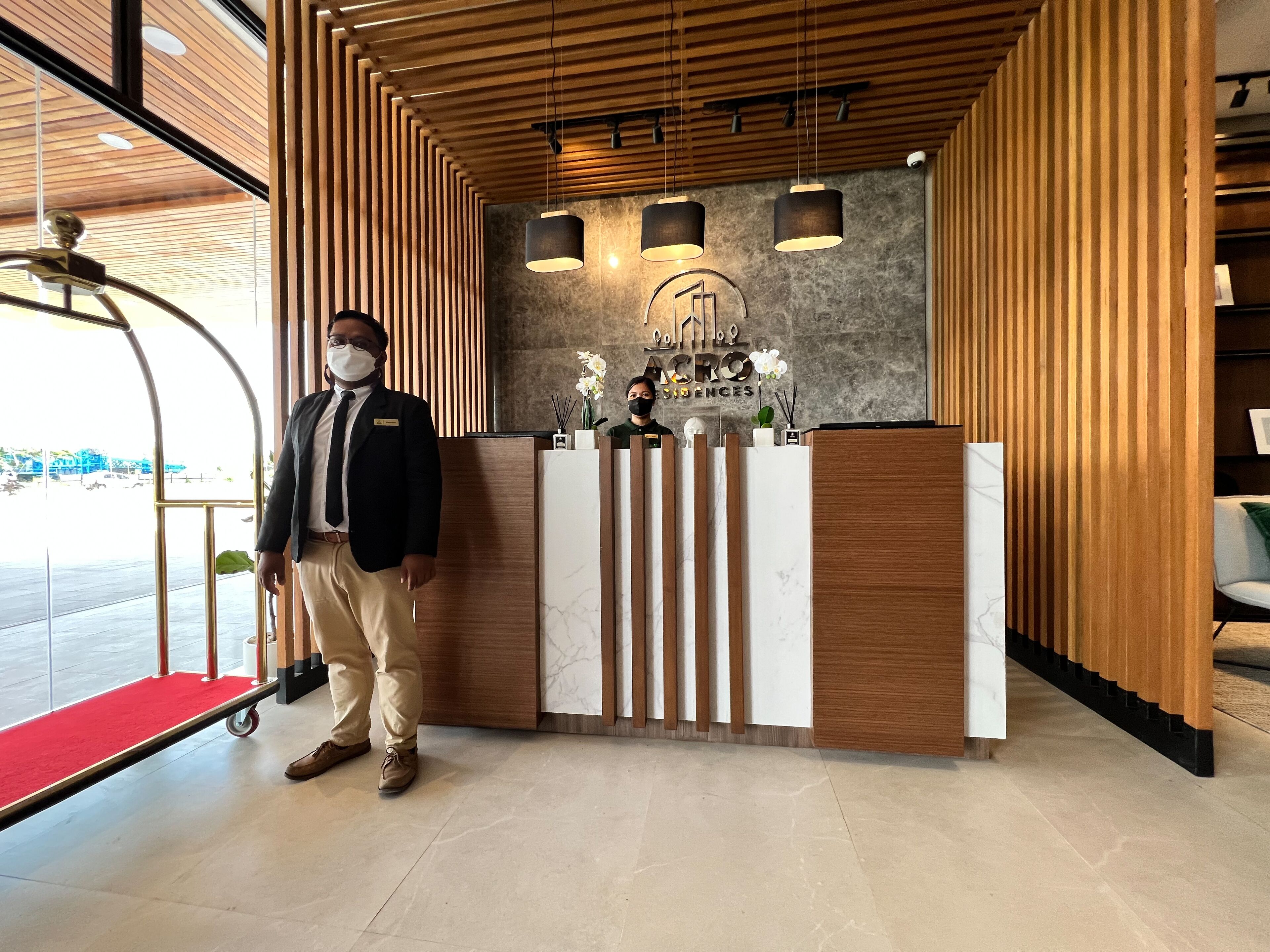 Uma área de recepção de hotel com um balcão de madeira, uma placa com o nome e um logotipo na parede.