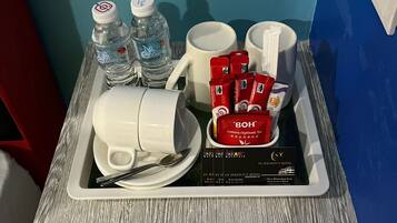 Uma bandeja com uma xícara, colher, duas garrafas de água e uma bandeja com sachês de chá vermelho em um ambiente de hotel.