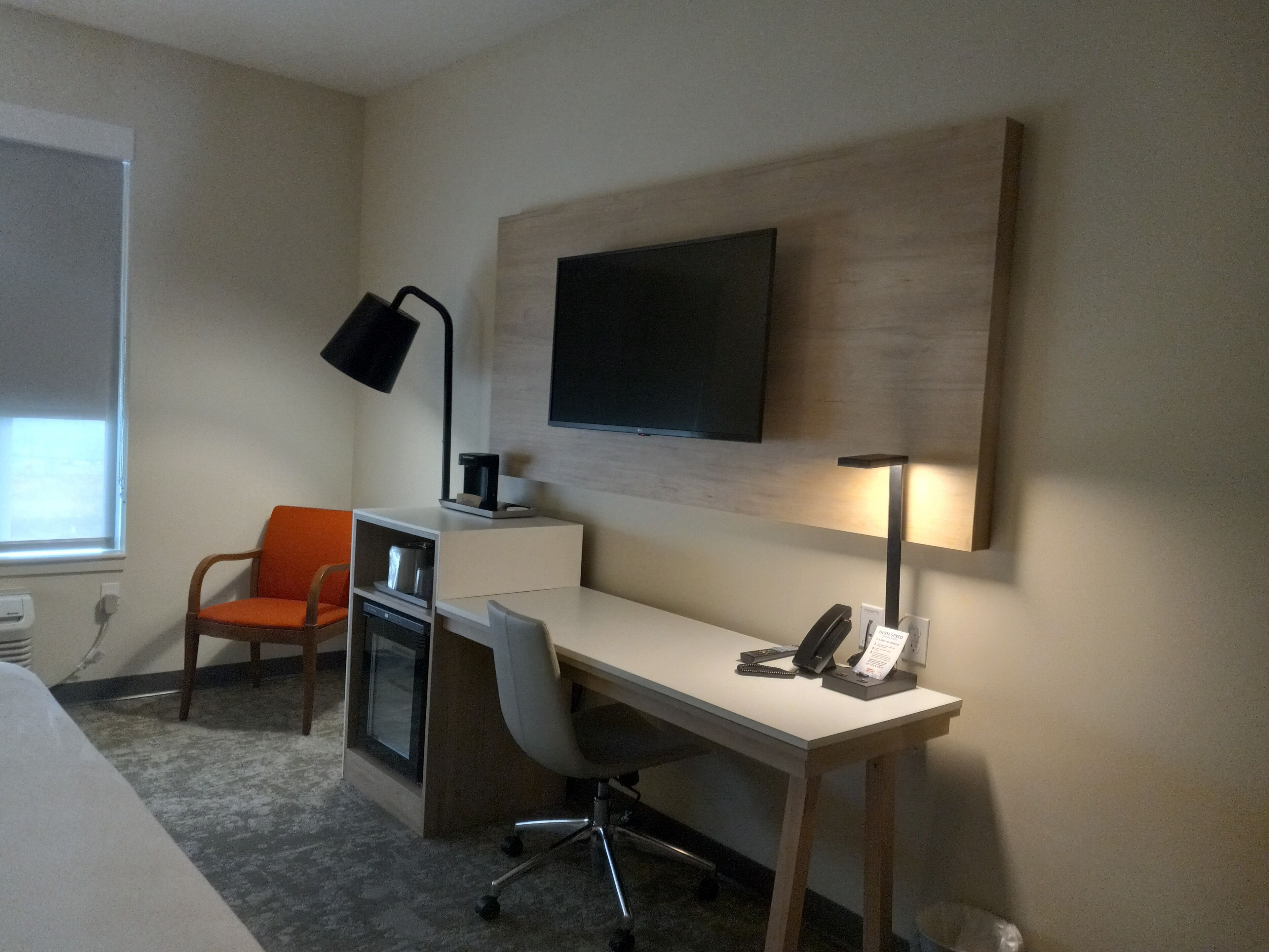 Quarto de hotel com escrivaninha, cadeira, TV e máquina de café.