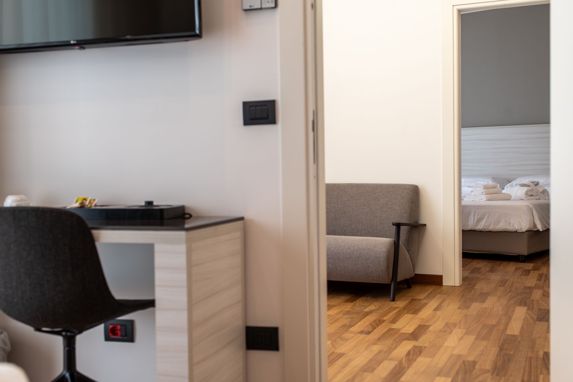 Quarto de hotel com uma cama, uma cadeira, uma escrivaninha e uma televisão fixada na parede.