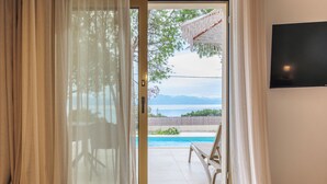 Quarto com porta de vidro deslizante para área da piscina, televisão na parede e vista para o exterior.