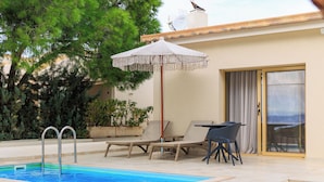 Uma piscina com área de descanso, incluindo uma mesa e cadeiras, e um guarda-sol coberto.