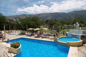 Piscina com espreguiçadeiras e guarda-sóis, rodeada por montanhas.