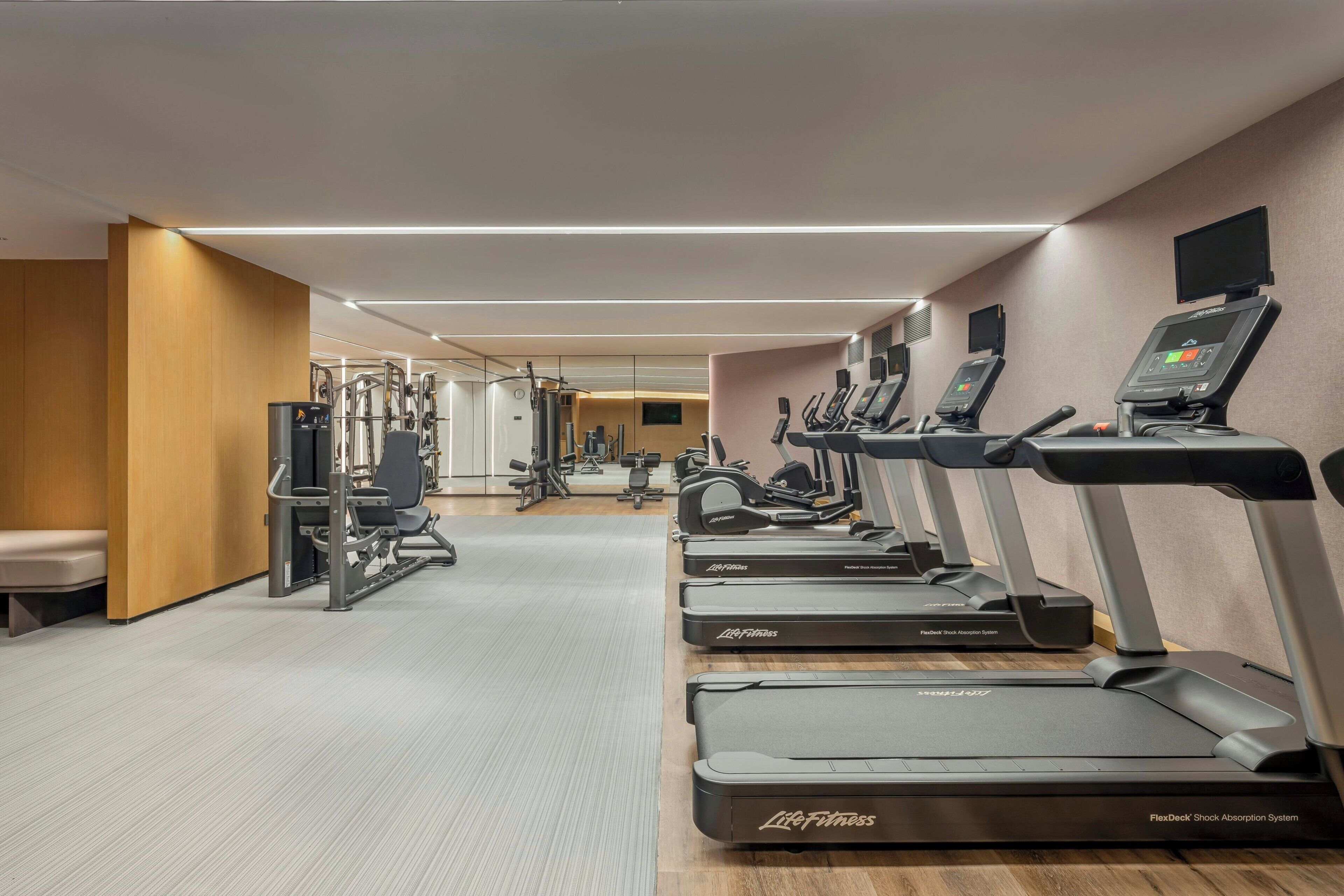 Academia com esteiras, máquinas de musculação e espelho.