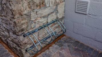Uma estante de metal fixada numa parede de pedra, uma abertura de ventilação na parede vizinha e um chão de tijolos.