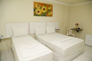 Quarto de hotel com duas camas, um quadro de girassóis na parede, uma mesinha com um vaso e um frigorífico.