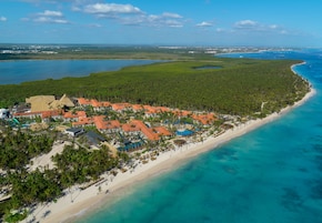 Vista aérea de um resort costeiro com vários edifícios, uma praia e águas azul-claras.