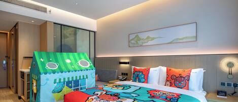 Quarto de hotel moderno com edredom colorido, casinha de brincar e uma grande janela.