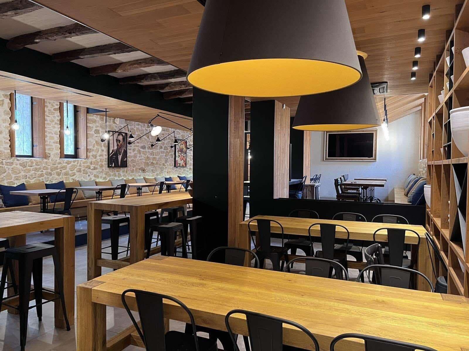 Um restaurante com mesas e cadeiras de madeira, paredes de pedra e luminárias pendentes.