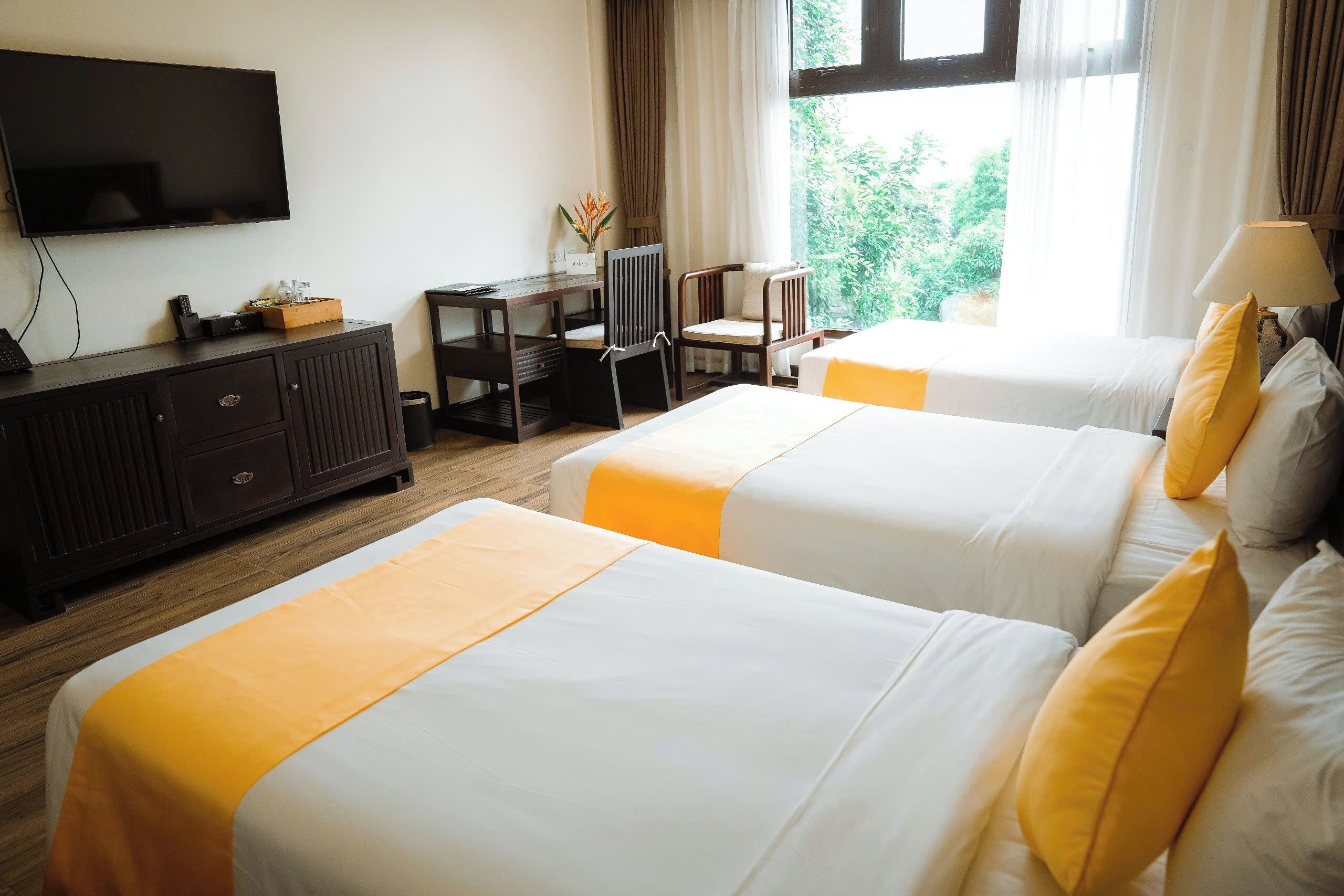 Quarto de hotel com duas camas, uma escrivaninha, uma televisão e uma janela com cortinas.