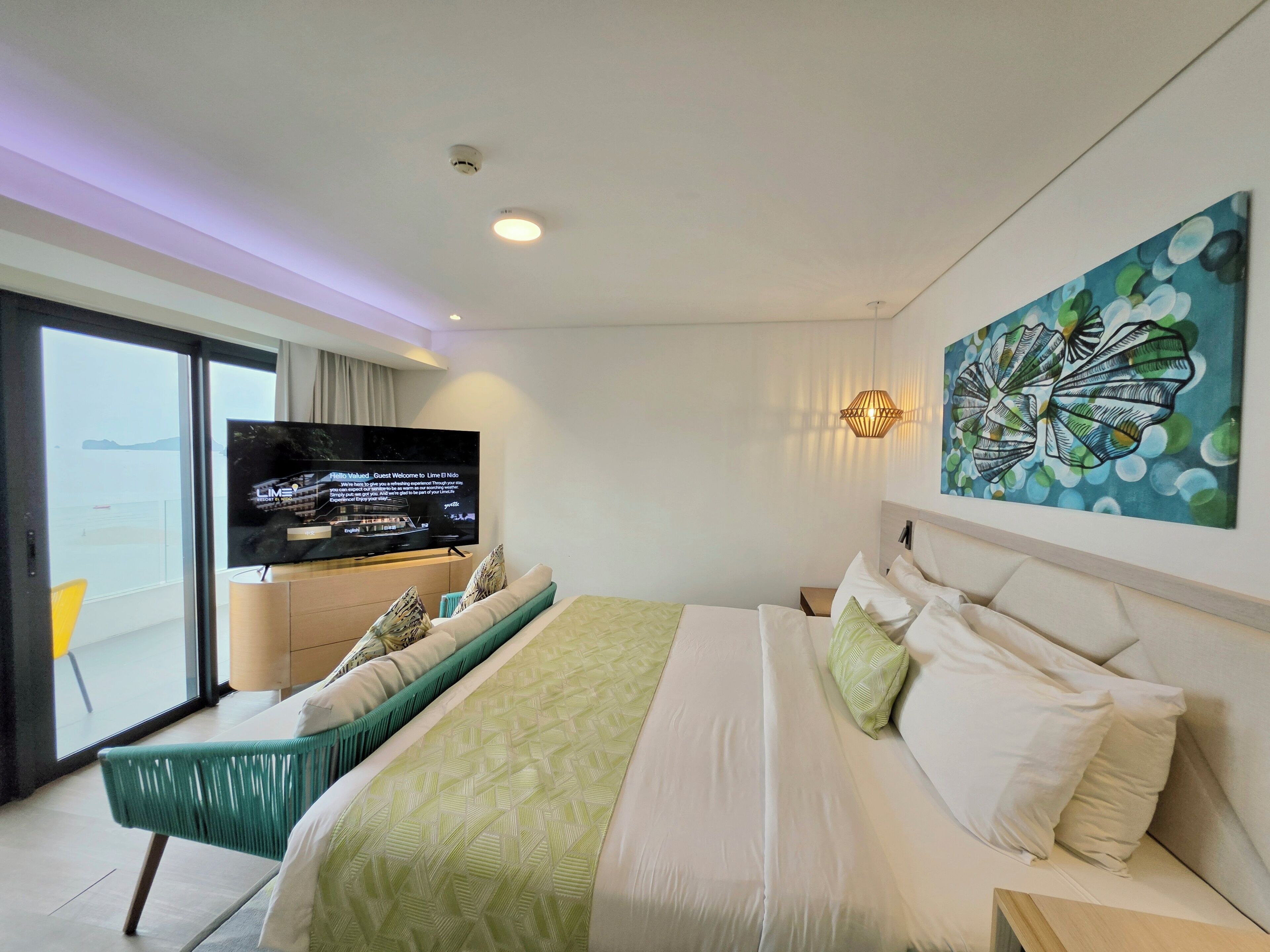 Quarto de hotel com cama, televisão, quadro e vista para o mar.