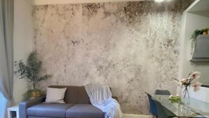 Uma sala de estar moderna com um sofá cinzento, uma mesa de jantar de vidro e uma parede com textura.