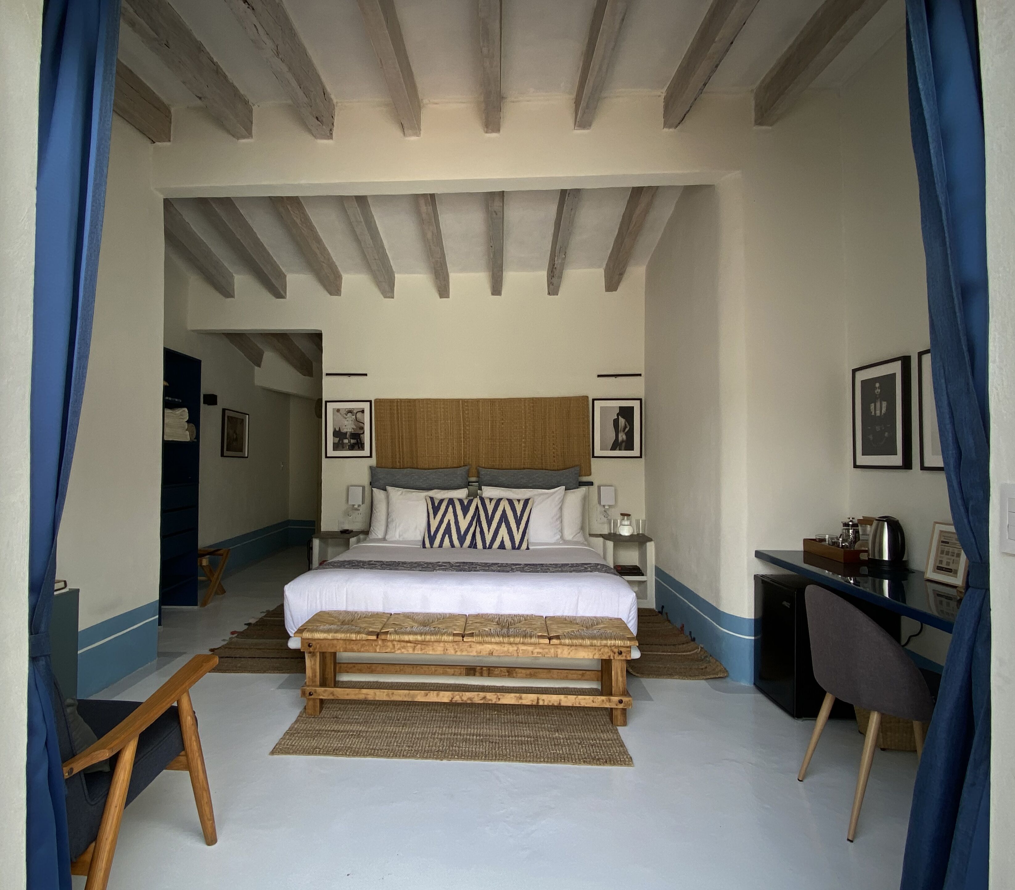Quarto com uma cama grande, um banco de madeira, uma escrivaninha e uma cadeira.