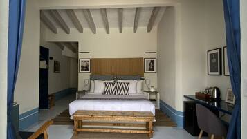 Quarto com uma cama grande, um banco de madeira, uma escrivaninha e uma cadeira.