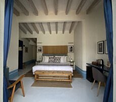 Quarto com uma cama grande, um banco de madeira, uma escrivaninha e uma cadeira.