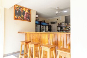 Uma área de bar com banquetas de madeira, um ventilador de teto e um quadro na parede.