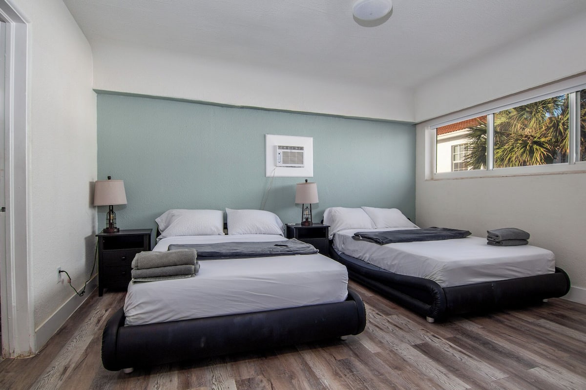 Quarto com duas camas, janela e ventilador de teto.