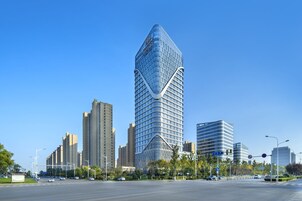 Um edifício moderno de arranha-céu com fachada de vidro curva, rodeado por outros edifícios altos e um céu azul límpido.