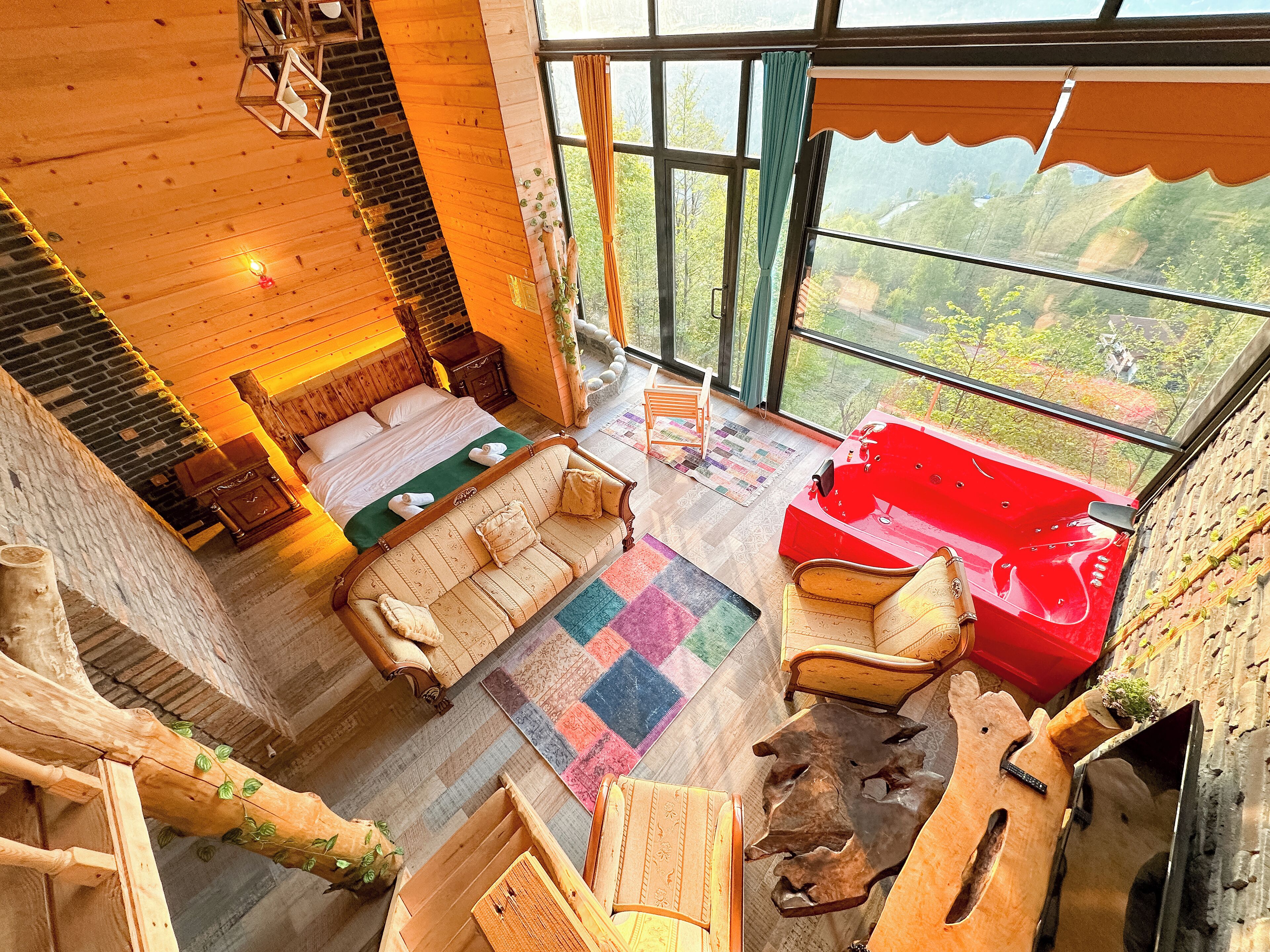 Quarto com pé-direito alto, uma cama grande, um sofá vermelho e vista para uma paisagem montanhosa através de amplas janelas.