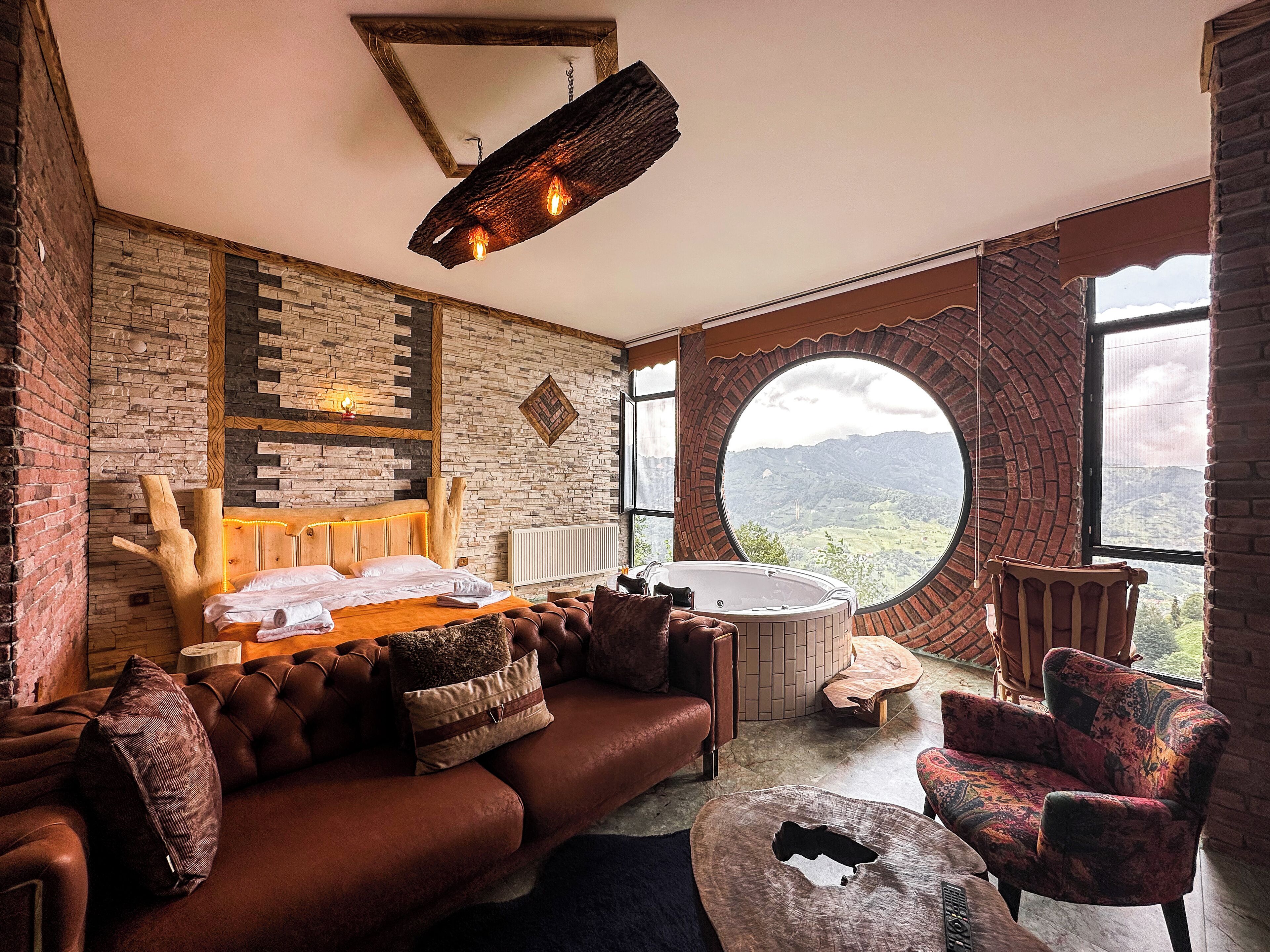 Quarto acolhedor com cama, sofá, poltrona e janela redonda com vista para as montanhas.