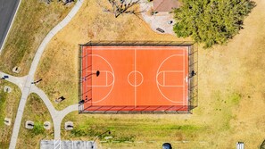 Vista aérea de uma quadra de basquete com caminhos e áreas verdes ao redor.