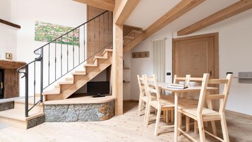 Uma escadaria de madeira com um patamar de pedra, uma sala de jantar com cadeiras e mesa de madeira, e um radiador na parede.