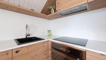 Cozinha moderna com pia preta, torneira de aço inoxidável, armários de madeira, forno embutido e bancada preta.