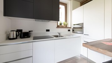 Uma cozinha moderna com armários brancos, uma pia de aço inoxidável, chaleira, torradeira e forno.