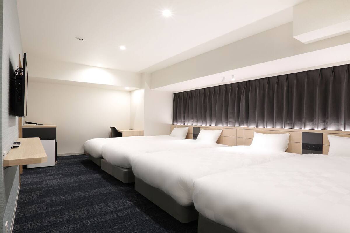 Quarto de hotel com uma cama grande, uma mesa, uma cadeira e uma TV fixada na parede.
