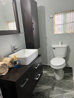 Casa de banho moderna com toucador de madeira escura, lavatório branco e sanita.