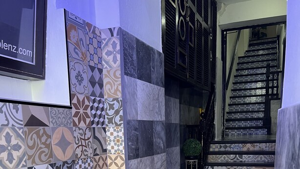 Uma escadaria com piso xadrez e uma parede com diversos desenhos em azulejo.
