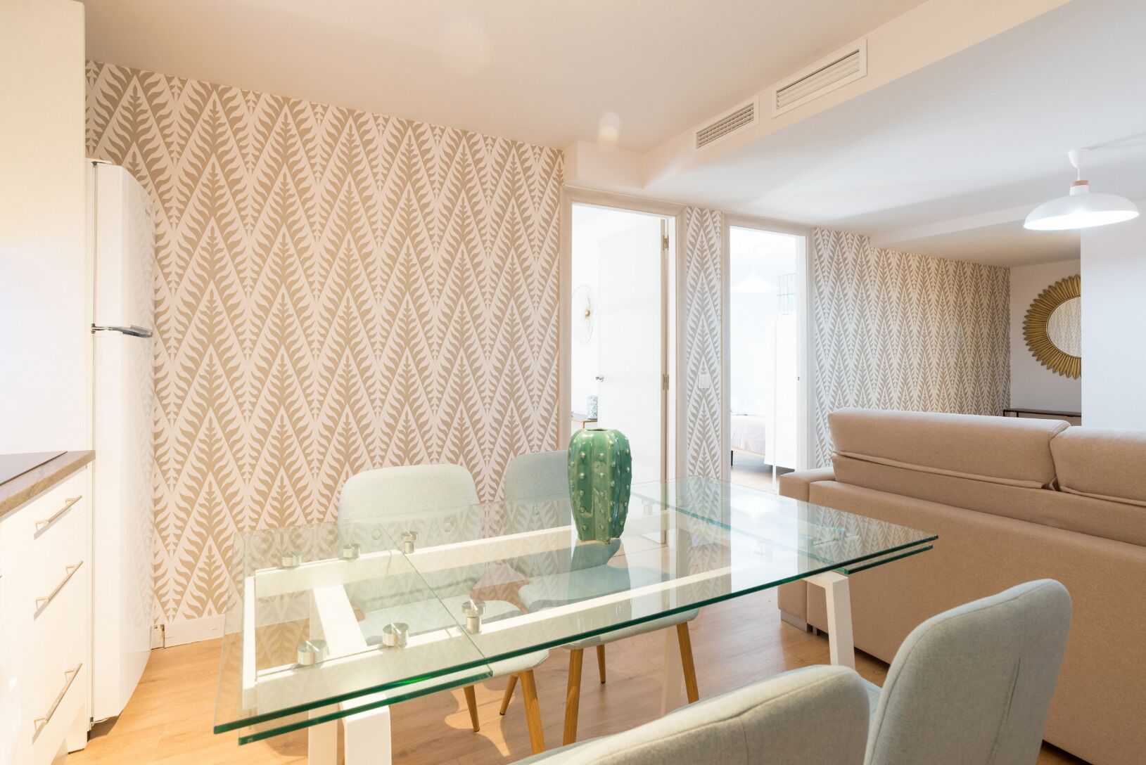 Uma sala de estar moderna com uma mesa de jantar de vidro, um sofá e papel de parede estampado.