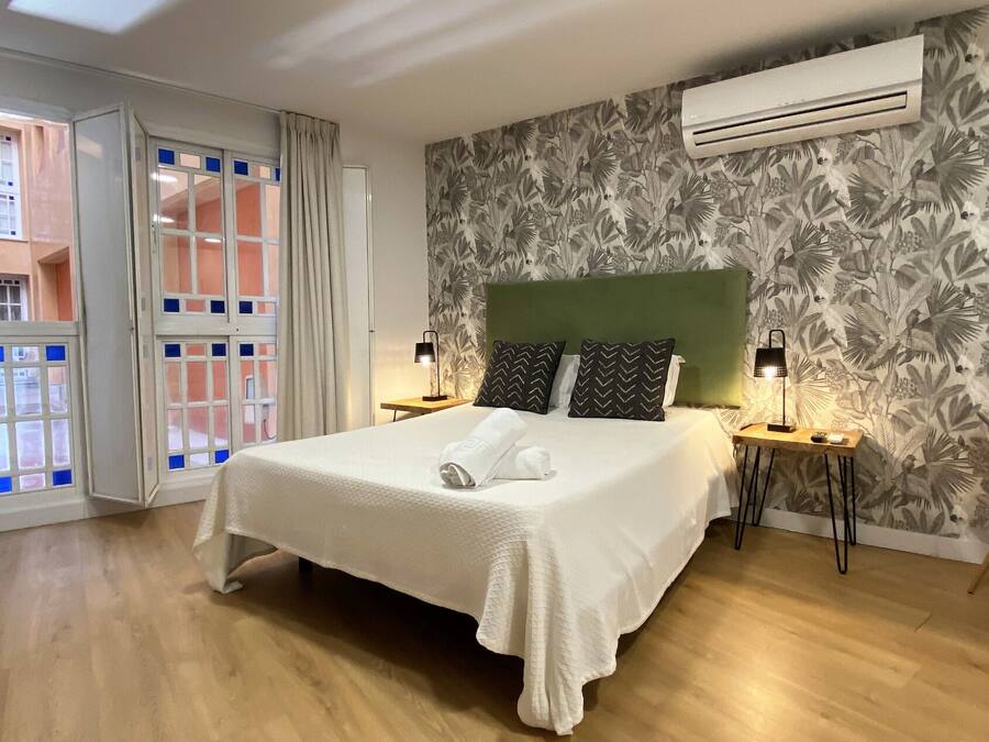 Quarto de hotel com cama, duas mesas de cabeceira com luminárias, ar condicionado e uma janela com cortinas.