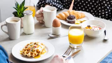 Uma mesa de café da manhã com um croissant, muffin e waffle, além de um copo de suco de laranja e uma garrafa de leite.