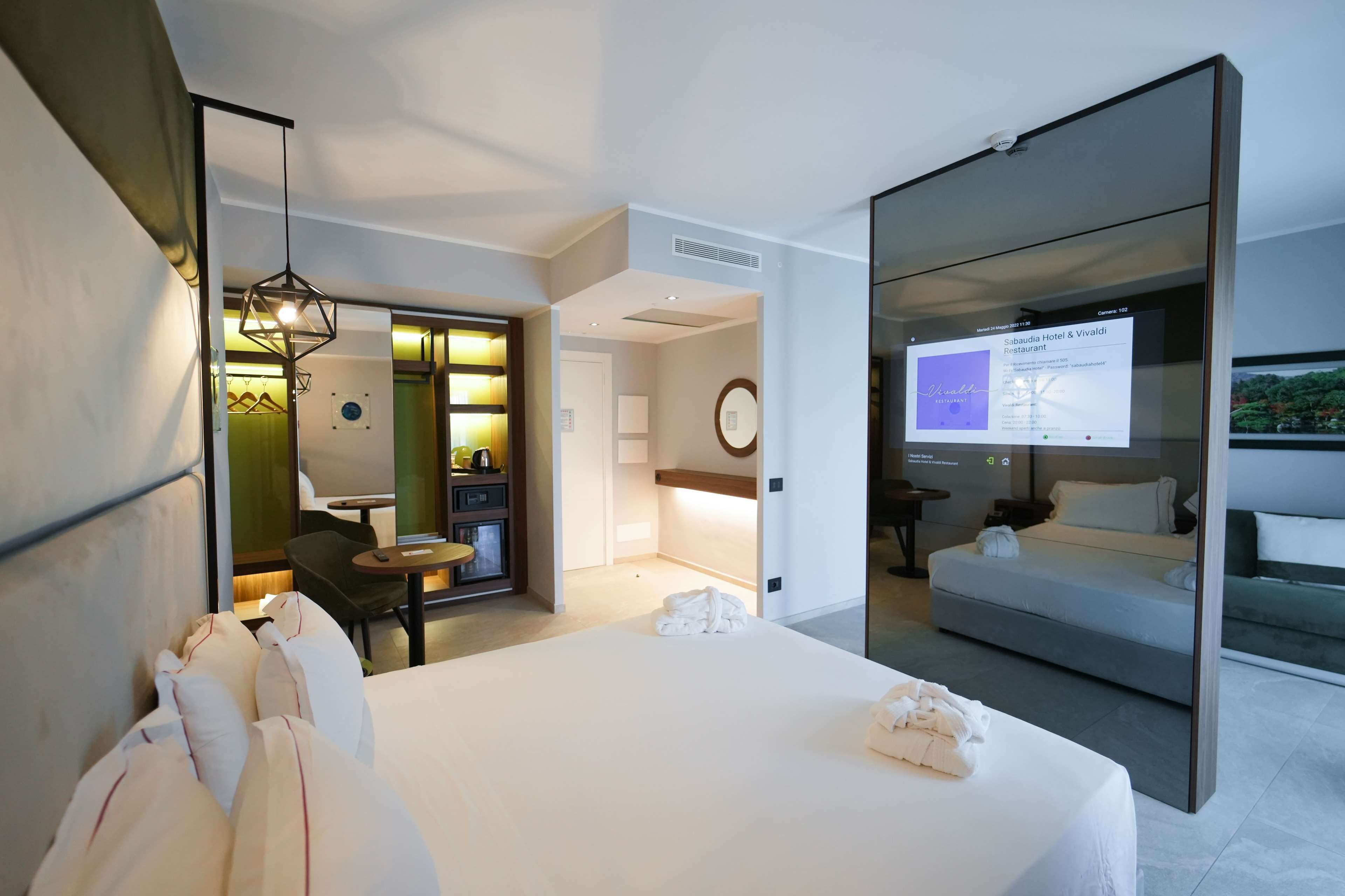 Quarto de hotel moderno com uma cama grande, uma escrivaninha, uma cadeira e uma televisão exibindo um mapa.