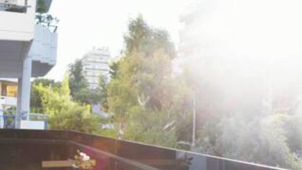Varanda com mesa e cadeiras, vista para um horizonte urbano com edifícios e árvores.