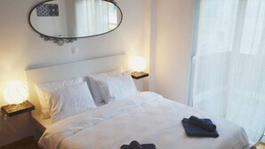 Quarto de hotel com uma cama grande, duas mesas de cabeceira com luminárias, um espelho fixado na parede e uma janela com cortinas leves.