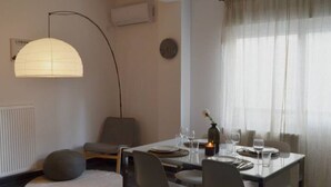 Uma sala de jantar com uma mesa posta para quatro pessoas, uma luminária de chão e uma janela com cortinas leves.